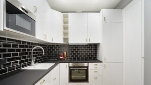 Uma cozinha moderna com armários brancos, bancada preta, forno de aço inoxidável e painel de azulejos preta e branca.