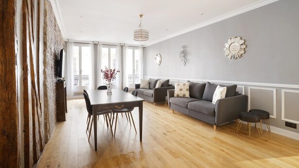 Uma sala de estar ampla com uma mesa de jantar de madeira, sofás cinzas e um candelabro.