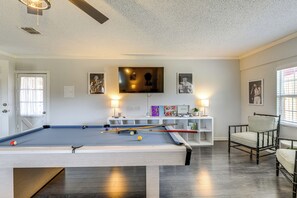 Uma mesa de bilhar com bolas de bilhar, um sofá e uma televisão fixada na parede.
