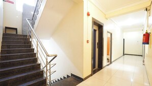 Um lobby de hotel limpo e moderno, com uma escadaria de mármore, um extintor de incêndio e um aviso de proibido o acesso.