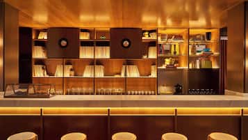 Uma área de bar com estantes de madeira, banquetas e uma vitrine com copos.