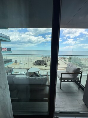 Uma varanda com vista para a praia, um sofá, uma mesa e uma placa.