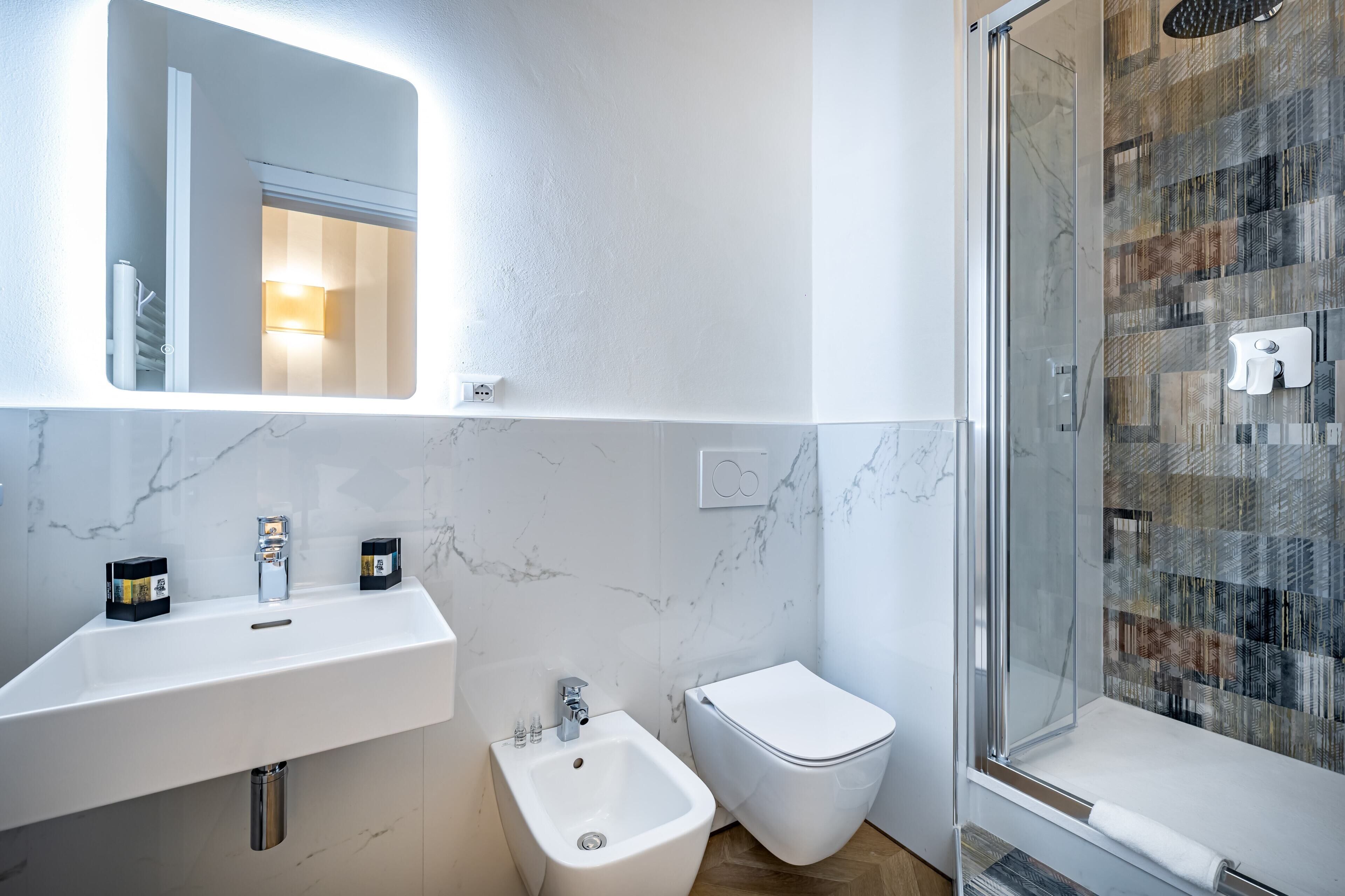 Uma casa de banho moderna com lavatório branco, bidé e cabine de duche em vidro.