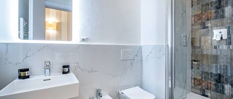 Uma casa de banho moderna com lavatório branco, bidé e cabine de duche em vidro.