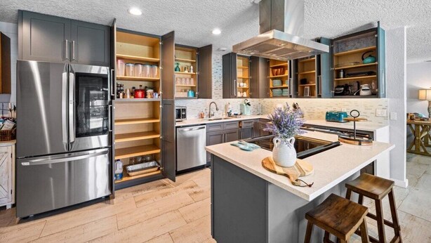 Cozinha moderna com frigorífico em aço inoxidável, prateleiras abertas e ilha central com banquetas.