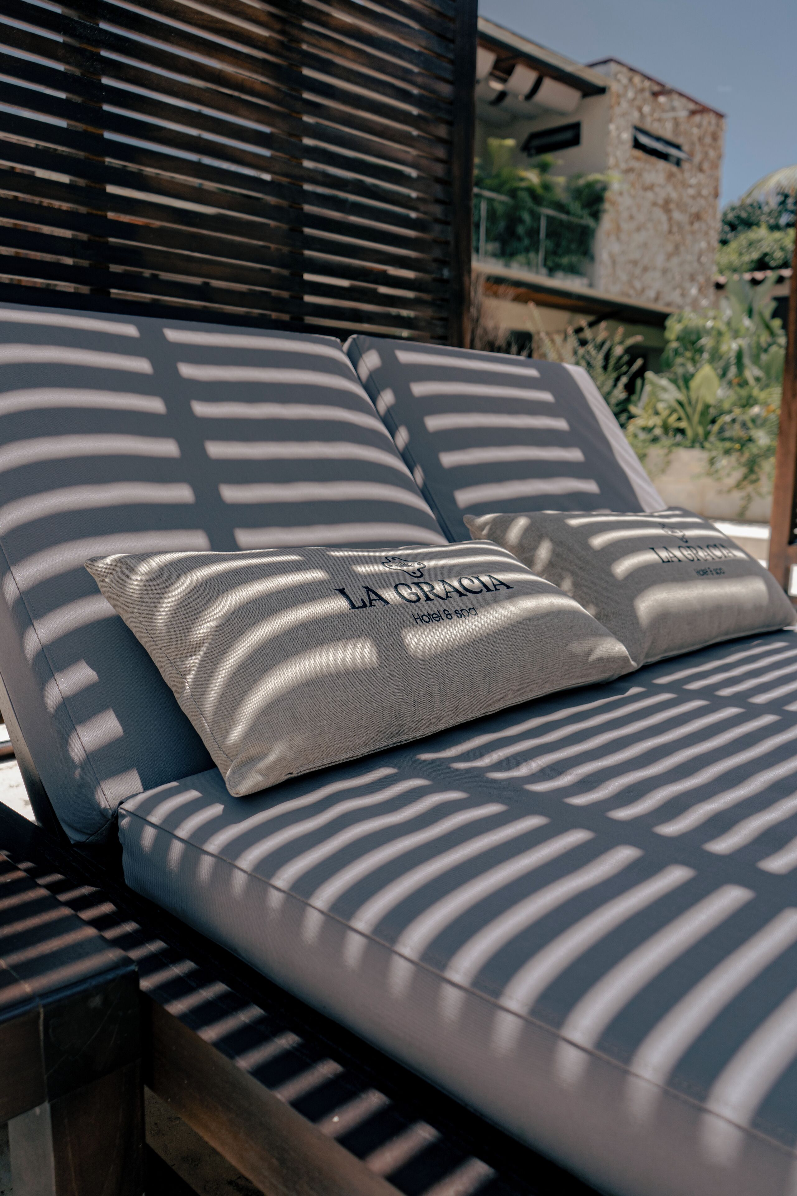 Uma cadeira de descanso com almofadas estampadas e um travesseiro com a inscrição "LA GRACIA Hotel & Spa".