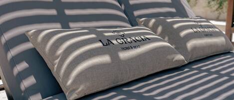 Uma cadeira de descanso com almofadas estampadas e um travesseiro com a inscrição "LA GRACIA Hotel & Spa".