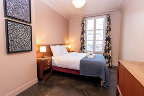 Quarto de hotel com uma cama, mesas de cabeceira, penteadeira e uma janela com cortinas.
