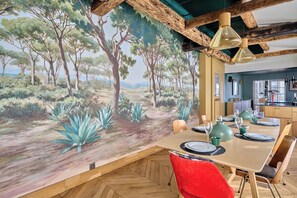 Uma área de refeições com um mural de uma cena florestal, vigas de madeira no teto e uma mesa posta para jantar.