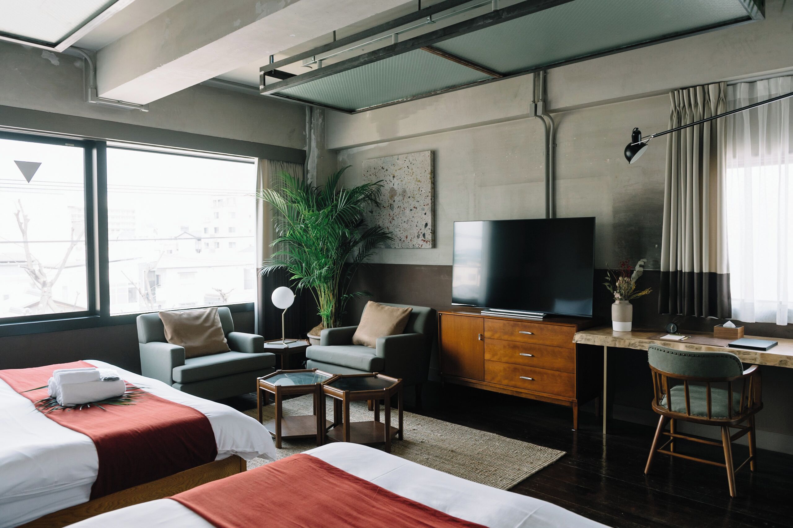Quarto de hotel com duas camas, televisão, escrivaninha e uma janela grande.