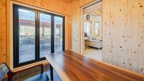 Interior de madeira com uma mesa grande, um banco e uma porta de vidro deslizante que dá para um pátio externo.
