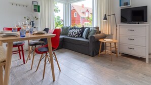 Uma sala de estar moderna com área de jantar, sofá, televisão e janela com vista para um edifício vermelho.