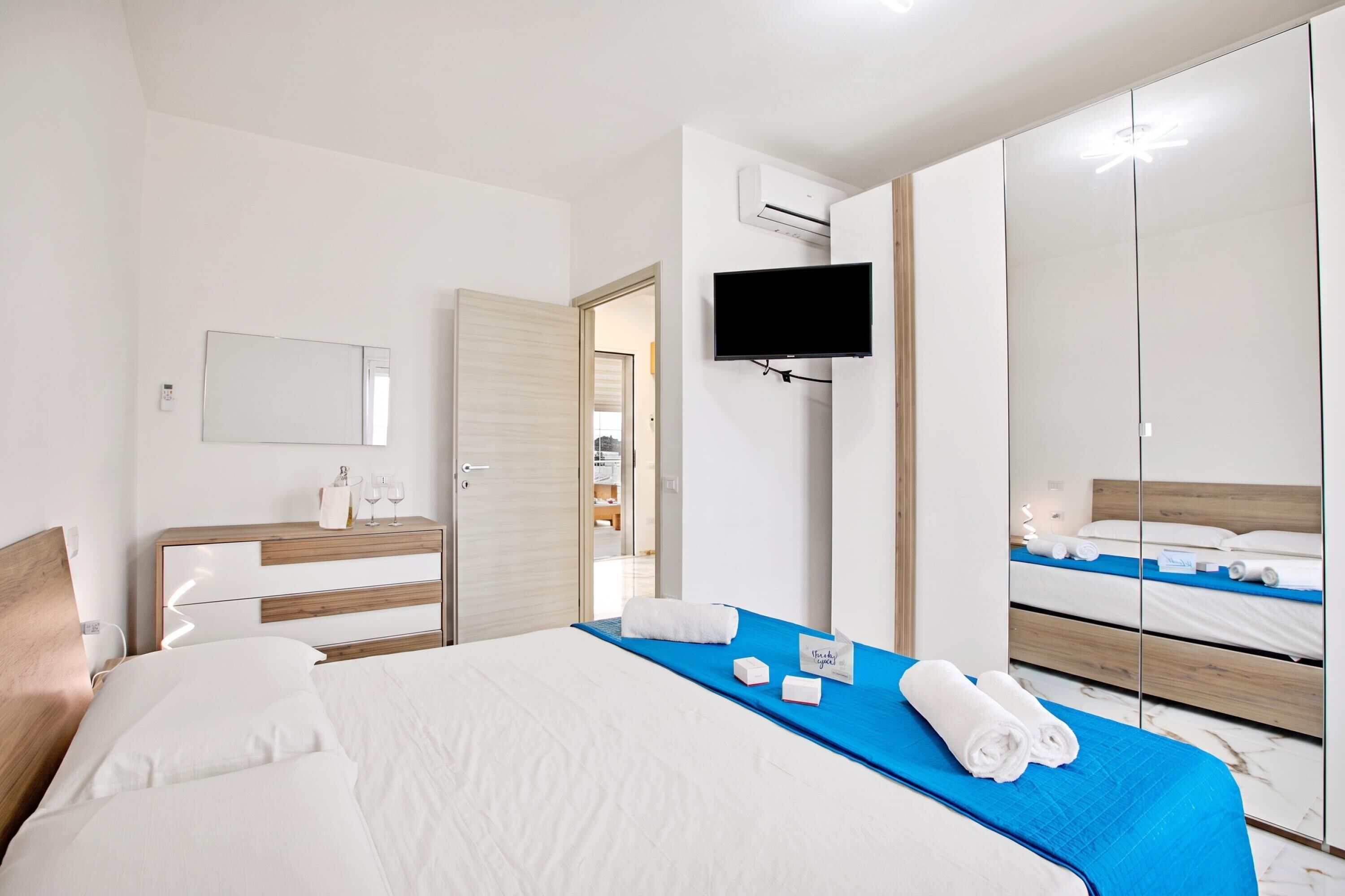 Quarto de hotel com cama, televisão, guarda-roupa e casa de banho visível através de uma porta aberta.