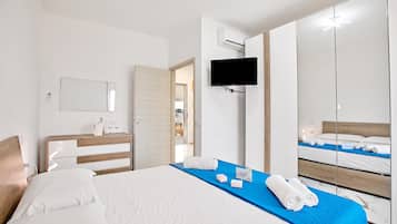 Quarto de hotel com cama, televisão, guarda-roupa e casa de banho visível através de uma porta aberta.