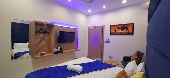 Quarto de hotel moderno com cama, televisão, guarda-roupa, uma pequena mesa com um vaso e um quadro na parede.