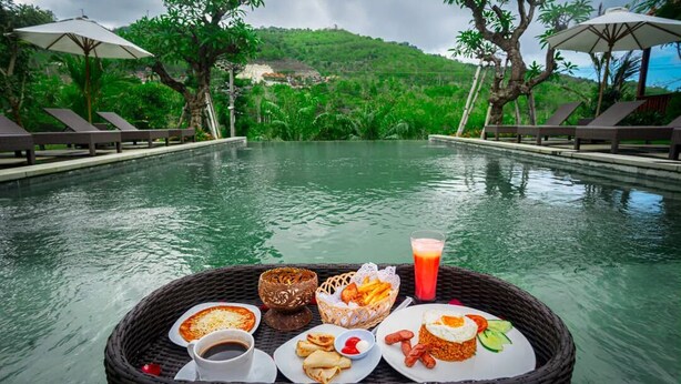 Disposição para refeições à beira da piscina, com uma bandeja de comida e bebidas, cercada por espreguiçadeiras e guarda-sóis.
