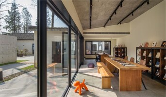 Uma biblioteca moderna com uma longa mesa de madeira, estantes e janelas amplas.
