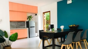 Uma cozinha moderna com armários cor de pêssego, uma geladeira preta e uma sala de jantar com mesa e cadeiras pretas.