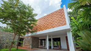 Um edifício moderno com fachada de tijolos, área de entrada coberta e vegetação ao redor.
