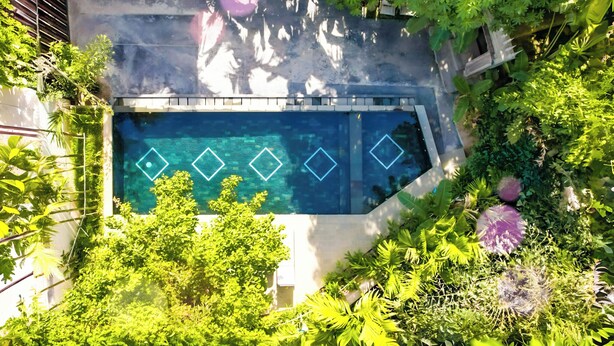 Uma piscina no terraço cercada por vegetação exuberante, com padrões geométricos na superfície da água.