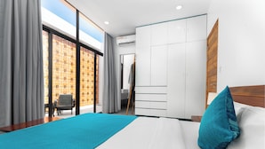 Quarto de hotel moderno com uma cama grande, vista para um edifício de tijolos, um guarda-roupa e uma mesa com cadeira.