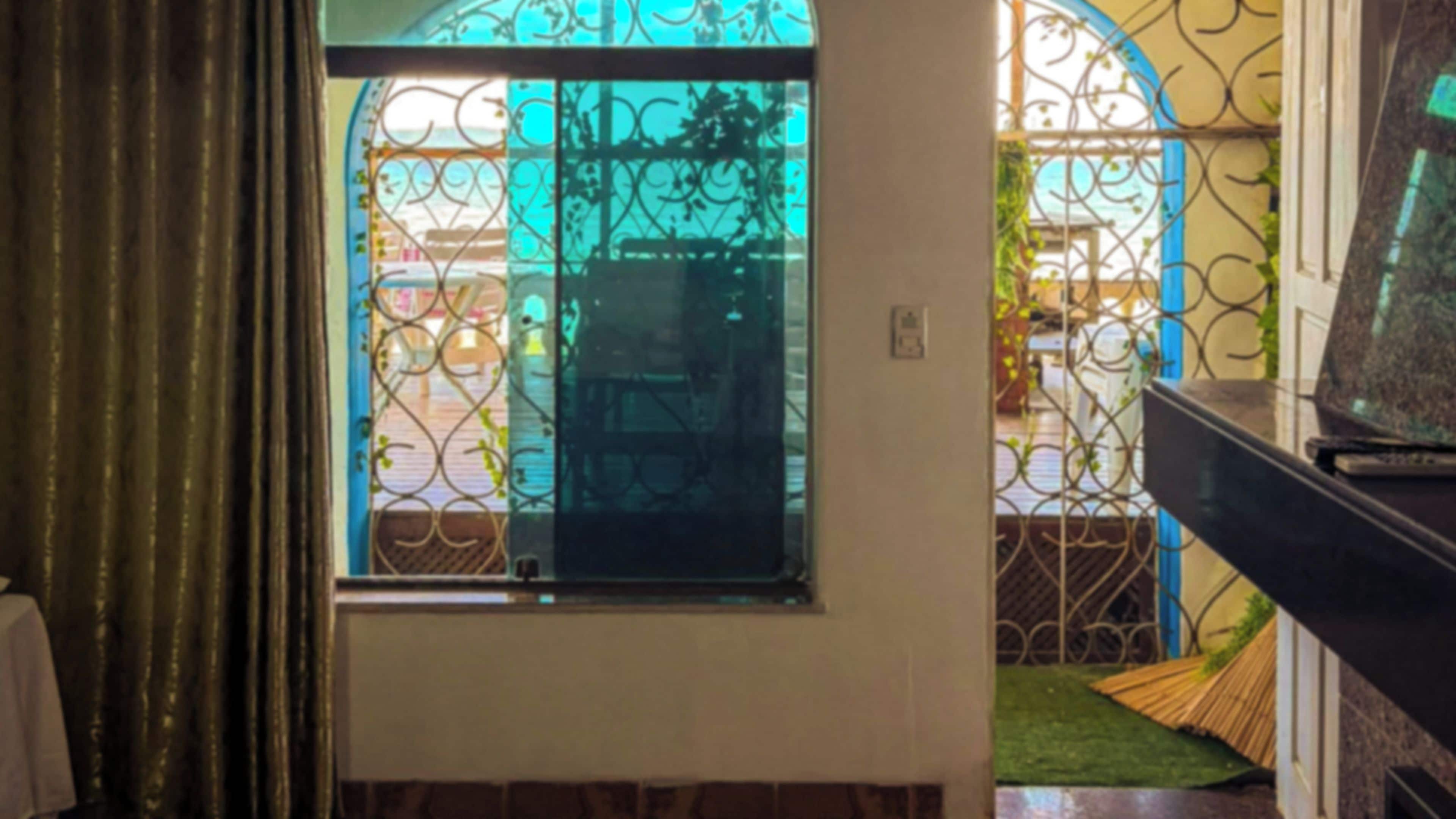 Quarto com janela que possui grades decorativas de metal, cortina e vista para uma varanda com corrimão.