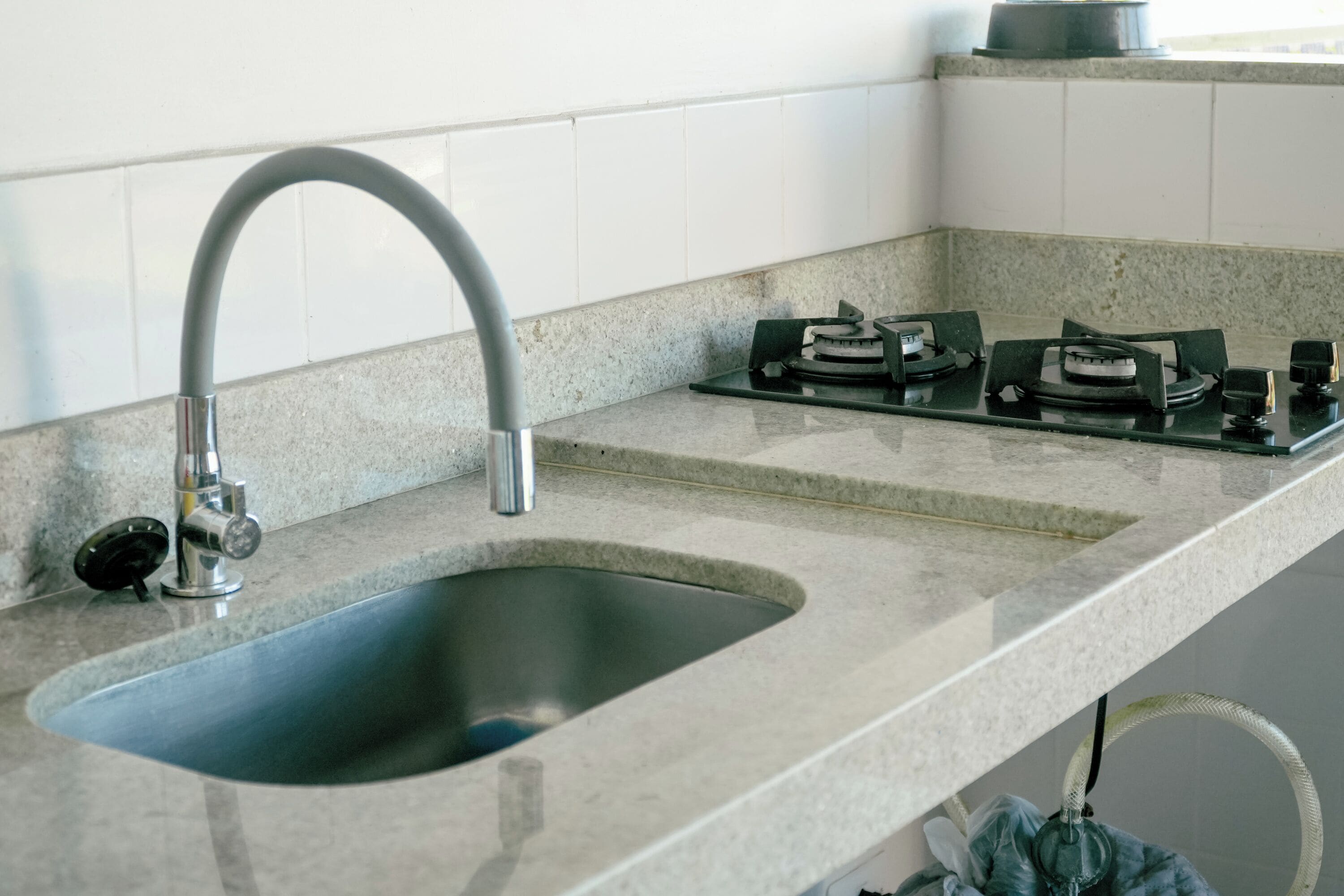 Uma cozinha com uma pia de aço inoxidável, uma torneira moderna e um fogão a gás.