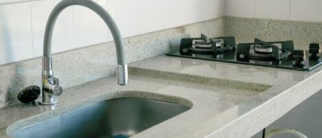 Uma cozinha com uma pia de aço inoxidável, uma torneira moderna e um fogão a gás.