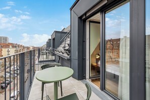 Varanda moderna com mesa e cadeiras verdes, porta de vidro que dá para um quarto e vista para a cidade.