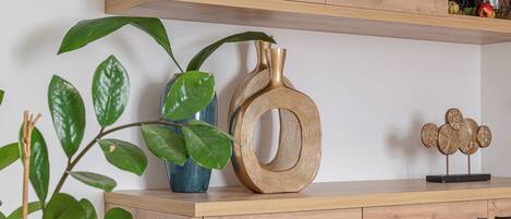 Um armário de madeira com duas gavetas e uma prateleira, acompanhado por um vaso de planta e objetos decorativos.