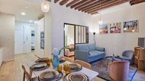 Uma sala de estar com área de jantar, mesa posta para quatro pessoas, sofá e televisão.