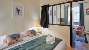 Quarto com cama, mesa de cabeceira com abajur, janela com cortinas e uma cadeira.