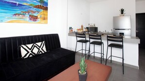Uma cozinha moderna com geladeira branca, área de refeições com banquetas e um sofá preto com almofada estampada.