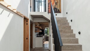 Interior moderno com escada, banco de madeira e área de cozinha ao fundo.