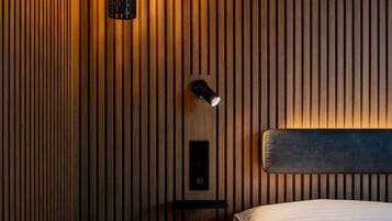 Quarto de hotel com parede de ripas de madeira, mesa de cabeceira com luminária e cama com cabeceira.