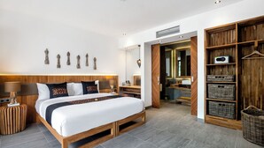 Quarto de hotel moderno com uma cama grande, cabeceira de madeira, mesas de cabeceira, guarda-roupa e banheiro visível através de uma porta aberta.