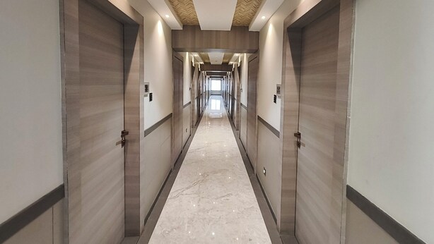Corredor moderno de hotel com painéis de madeira no teto, piso de mármore e portas em ambos os lados.