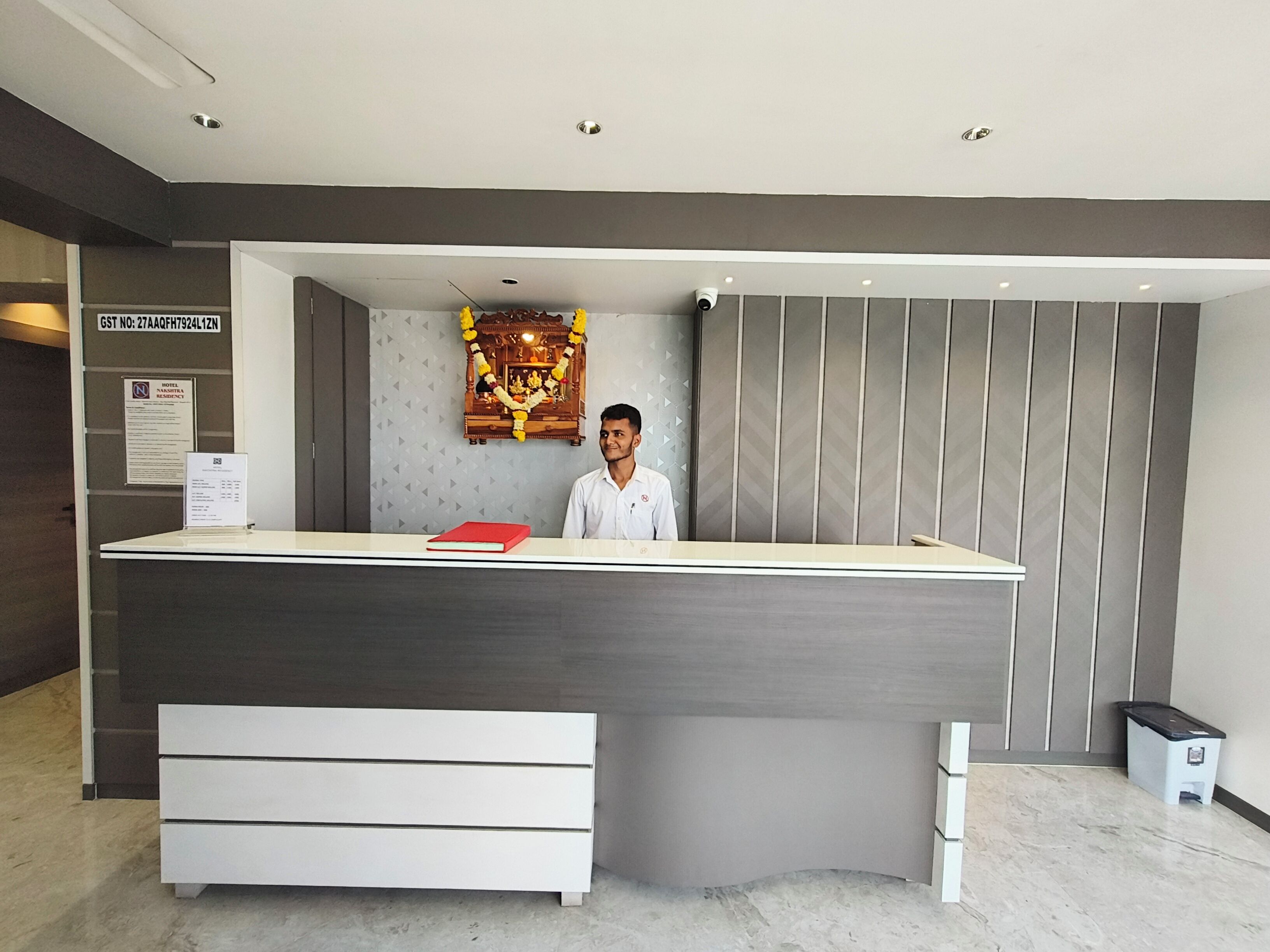 Uma receção de hotel com design moderno, um ecrã digital e um pequeno contentor de lixo à direita.