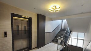 Um interior moderno com piso de mármore, escada com guarda-corpos de vidro e elevador embutido na parede.