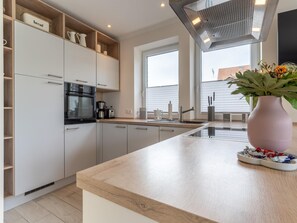 Uma cozinha moderna com armários brancos, forno embutido, cafeteira e um vaso com flores na bancada.