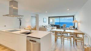 Uma cozinha moderna com ilha central, máquina de lavar louça embutida e uma grande janela com vista para o mar.