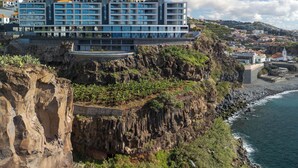 Um hotel moderno com vários andares, localizado em um penhasco com vista para o mar.