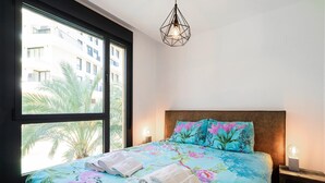Quarto com uma grande janela, cama com roupa de cama florida e luminária pendente.