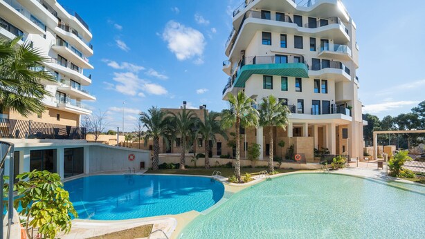 Um hotel moderno com uma grande piscina, várias varandas e palmeiras.