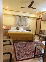 Um quarto com cama, ventoinha no teto, mesa de cabeceira, cadeira, escrivaninha e guarda-roupa.