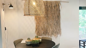 Mesa de jantar redonda com quatro cadeiras, luminária pendente trançada e um painel de parede tecido.