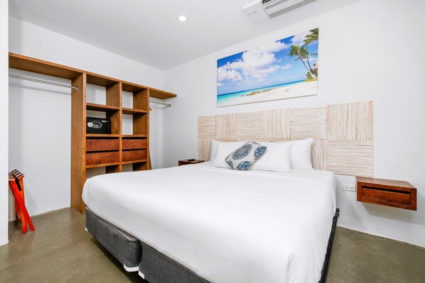 Quarto com cama, prateleiras de madeira, pintura de uma praia e um pequeno criado-mudo de madeira.