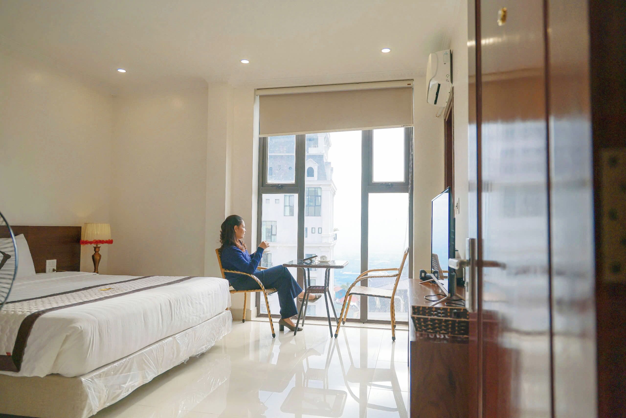 Quarto de hotel com cama, escrivaninha e cadeira. Janela com vista para edifícios.