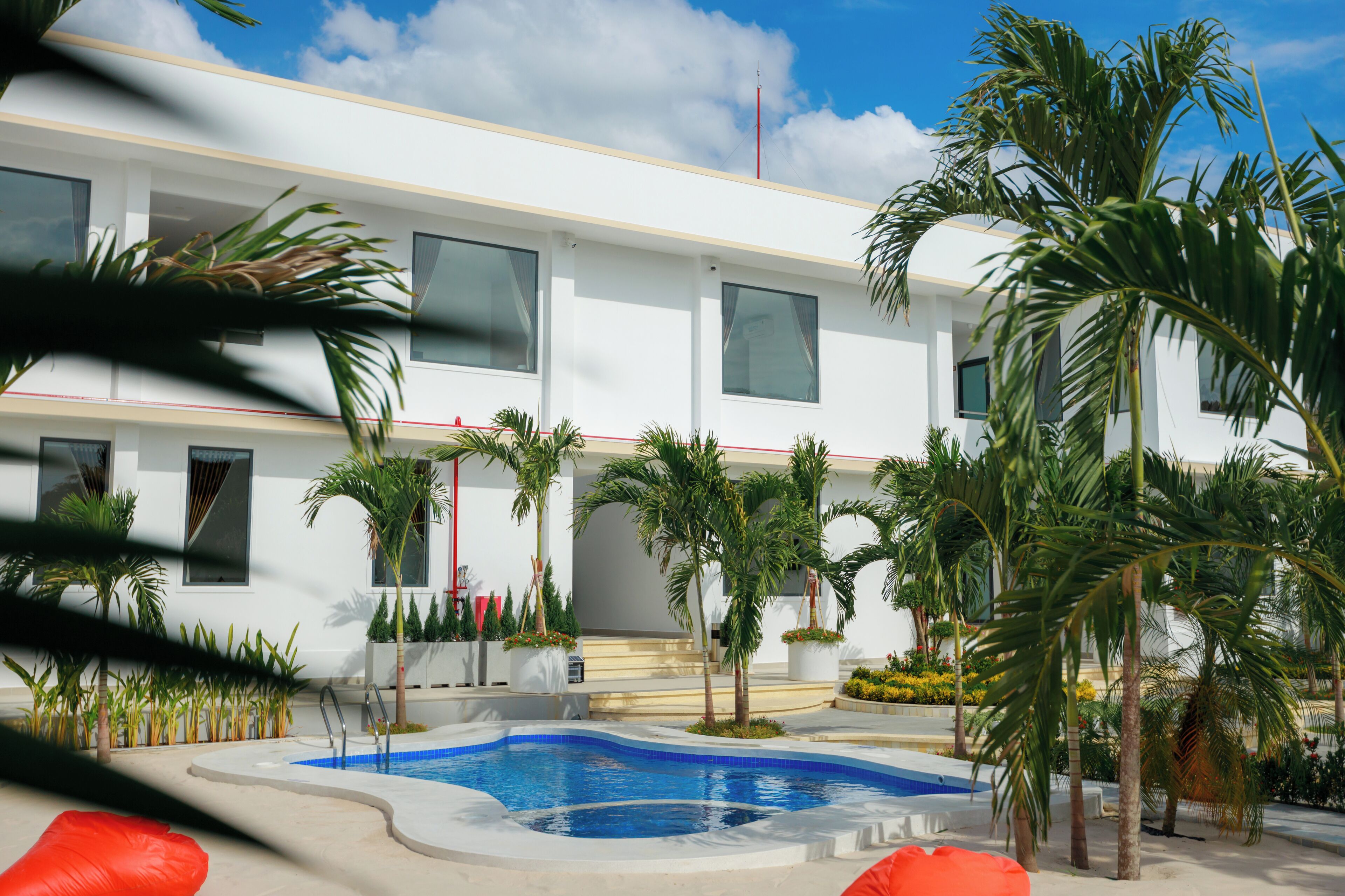 Um edifício moderno com piscina, rodeado por palmeiras e plantas.
