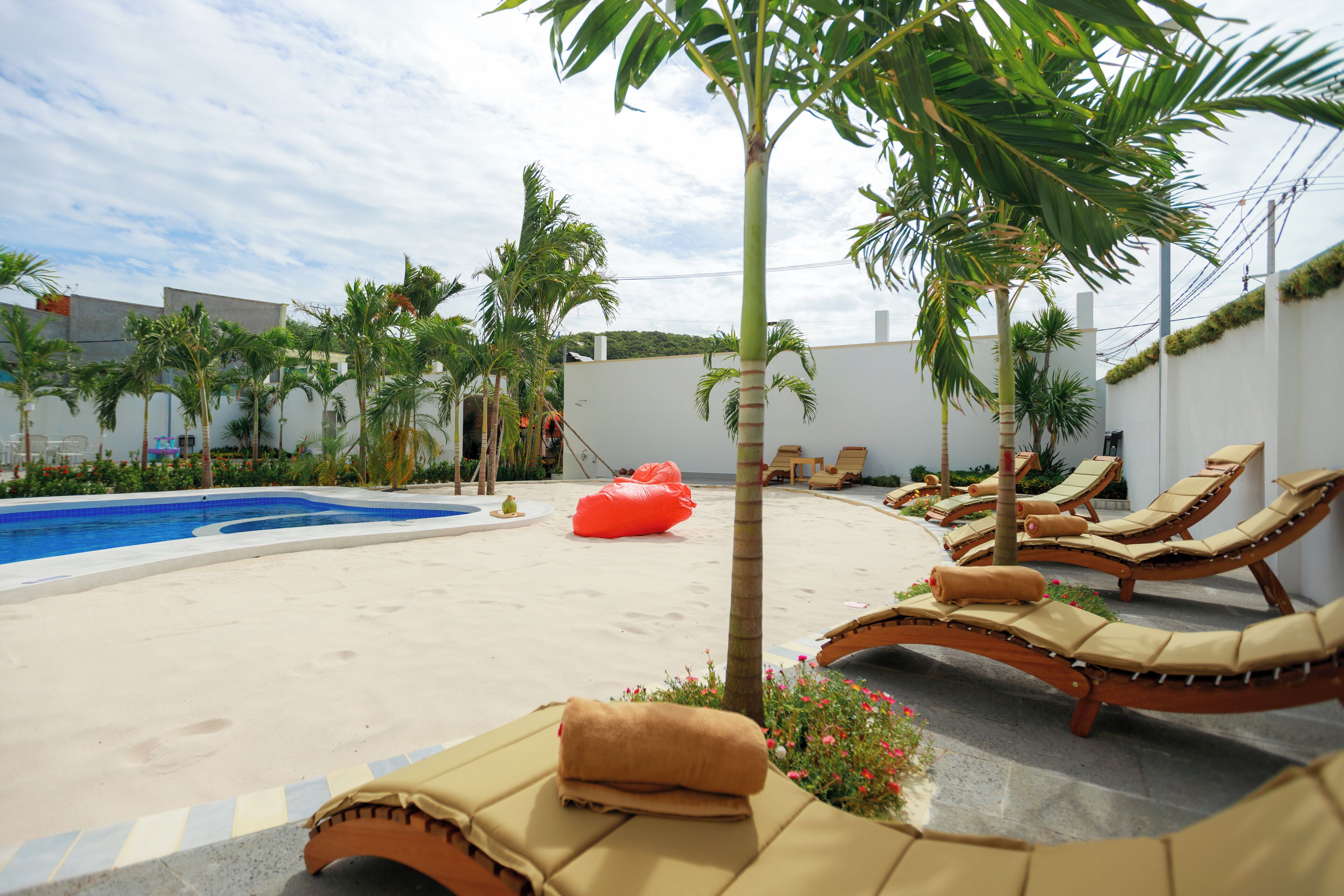 Área de piscina com espreguiçadeiras, uma piscina pequena e palmeiras.